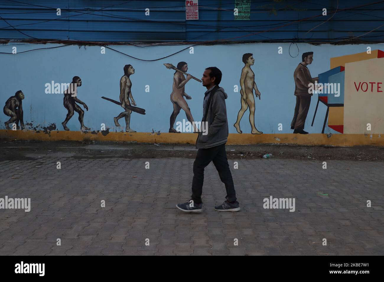 An indian man walking past the evolution of human mural, which also ...
