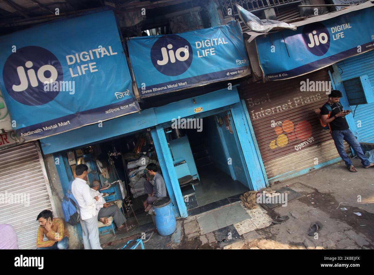 People stand in front of a shop with an advertisement of Reliance Jio ...
