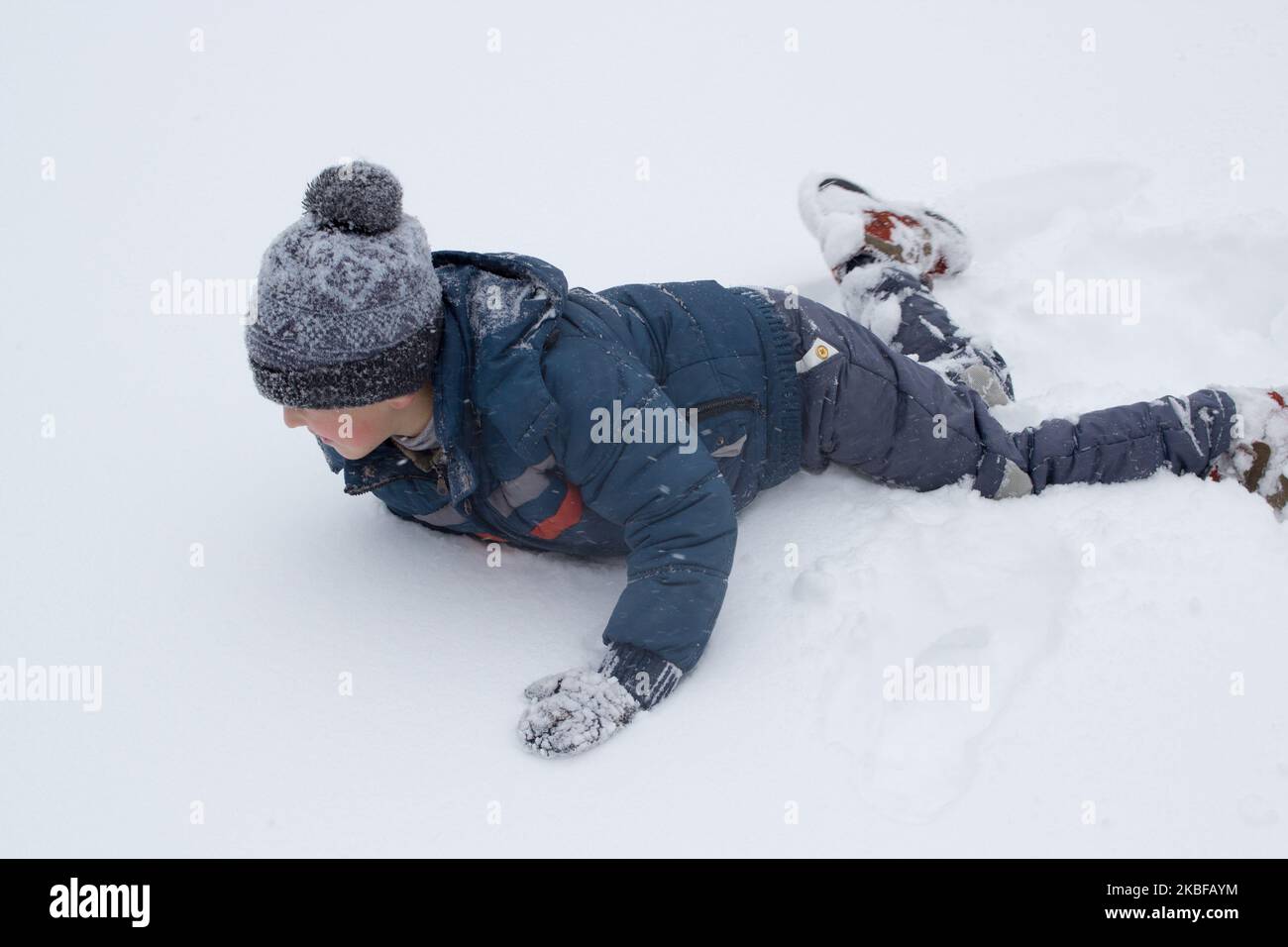 a funny boy fell on the snow and lying on his stomach Stock Photo - Alamy