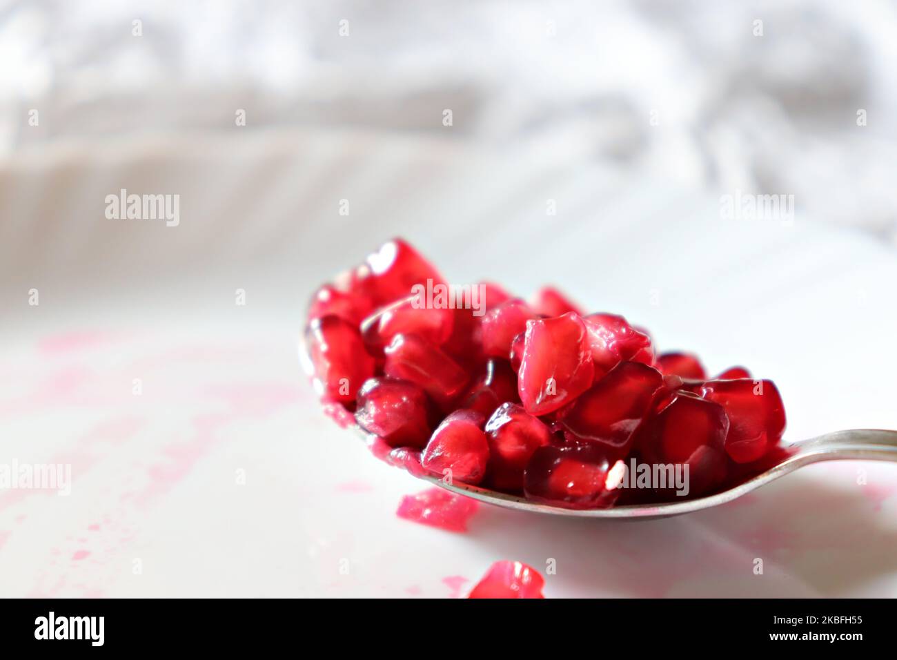 Close-up of pomegranate fruit seeds in a spoon against white background ...
