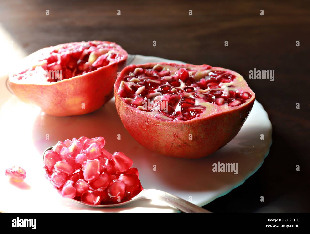 Close-up of pomegranate fruit seeds in a spoon on a wooden table ...