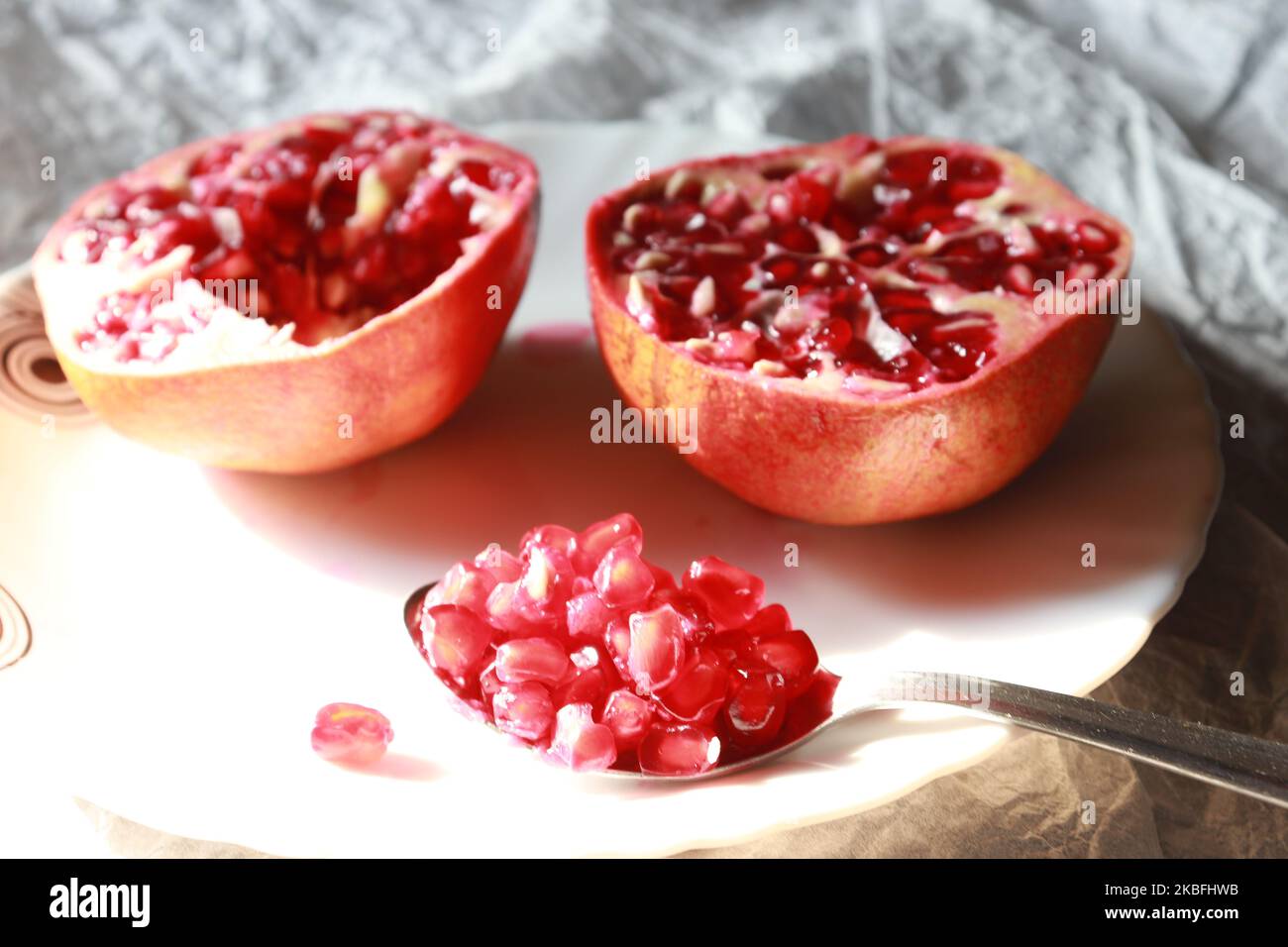 Close-up of pomegranate fruit seeds in a spoon against white background ...