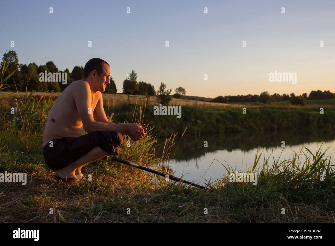 sitting man with a fishing rod and fishing in the lake Stock Photo - Alamy