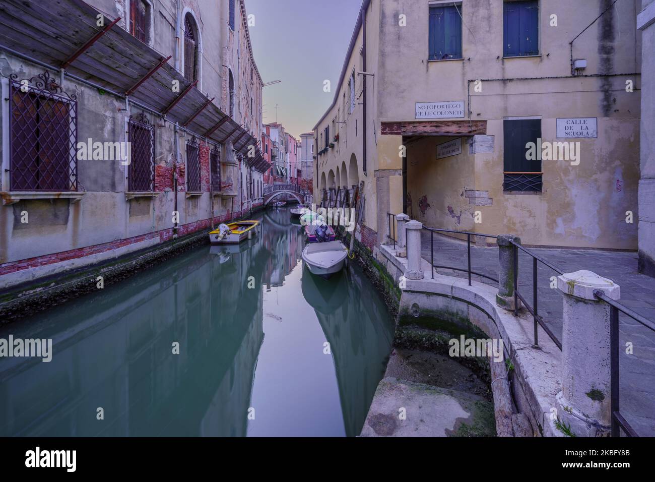 Sunrise view of canal, boats, bridge, and street name signs, in Venice ...