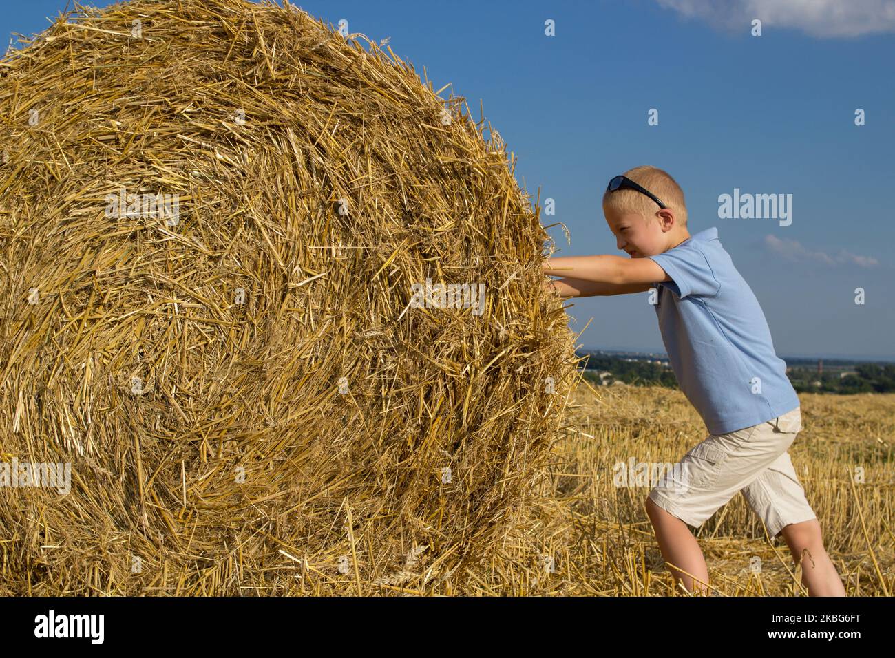 young boy posing outdoor pushing a round haystack and looking away ...