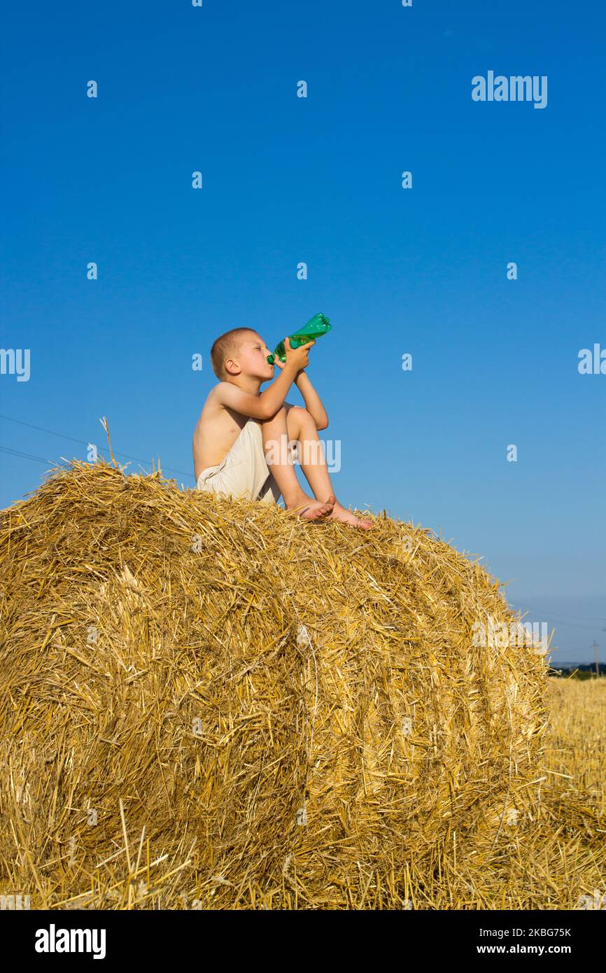 The boy sat on a bale of hay and drank water from a bottle Stock Photo ...