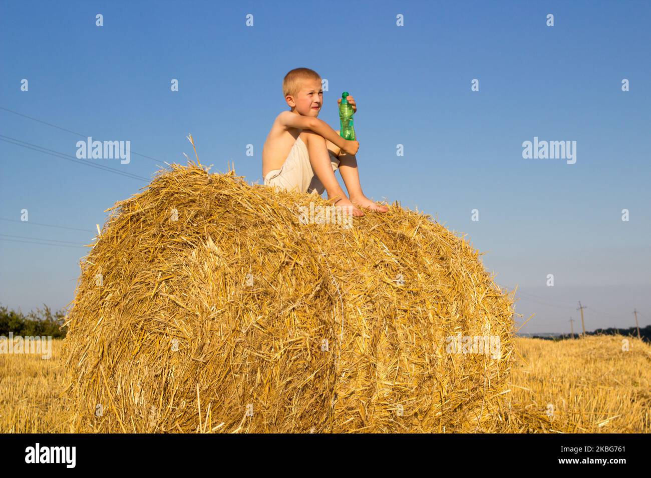 The young boy sat on a bunch of hay and held a bottle of water Stock ...