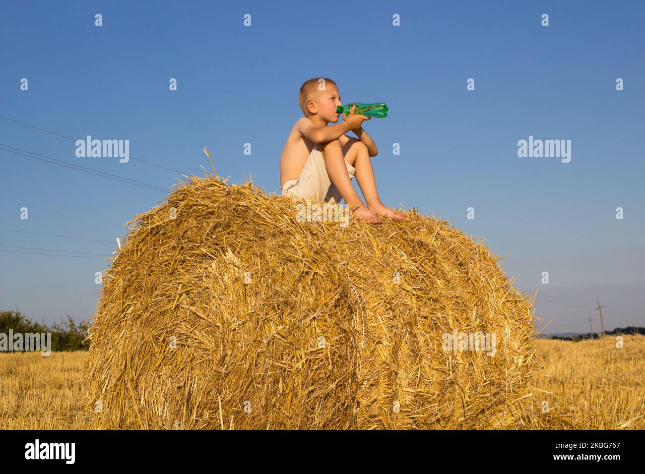 The boy sat in the field in the bundles of hay and drank water Stock ...
