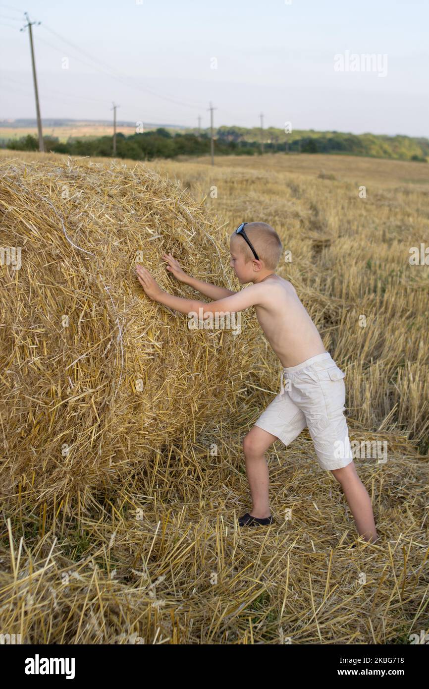 Childhood. Boy at hay bale, summer. Boy play on farm or ranch field ...