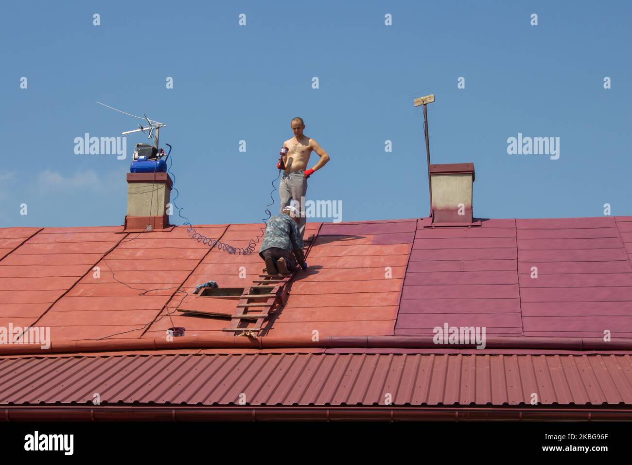 two men painted red roof air compressor Stock Photo - Alamy