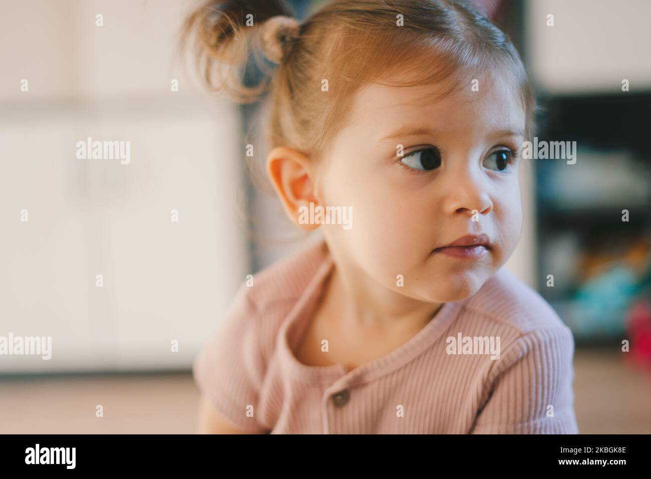 Portrait of an adorable baby with two pigtails looking seriously to one ...