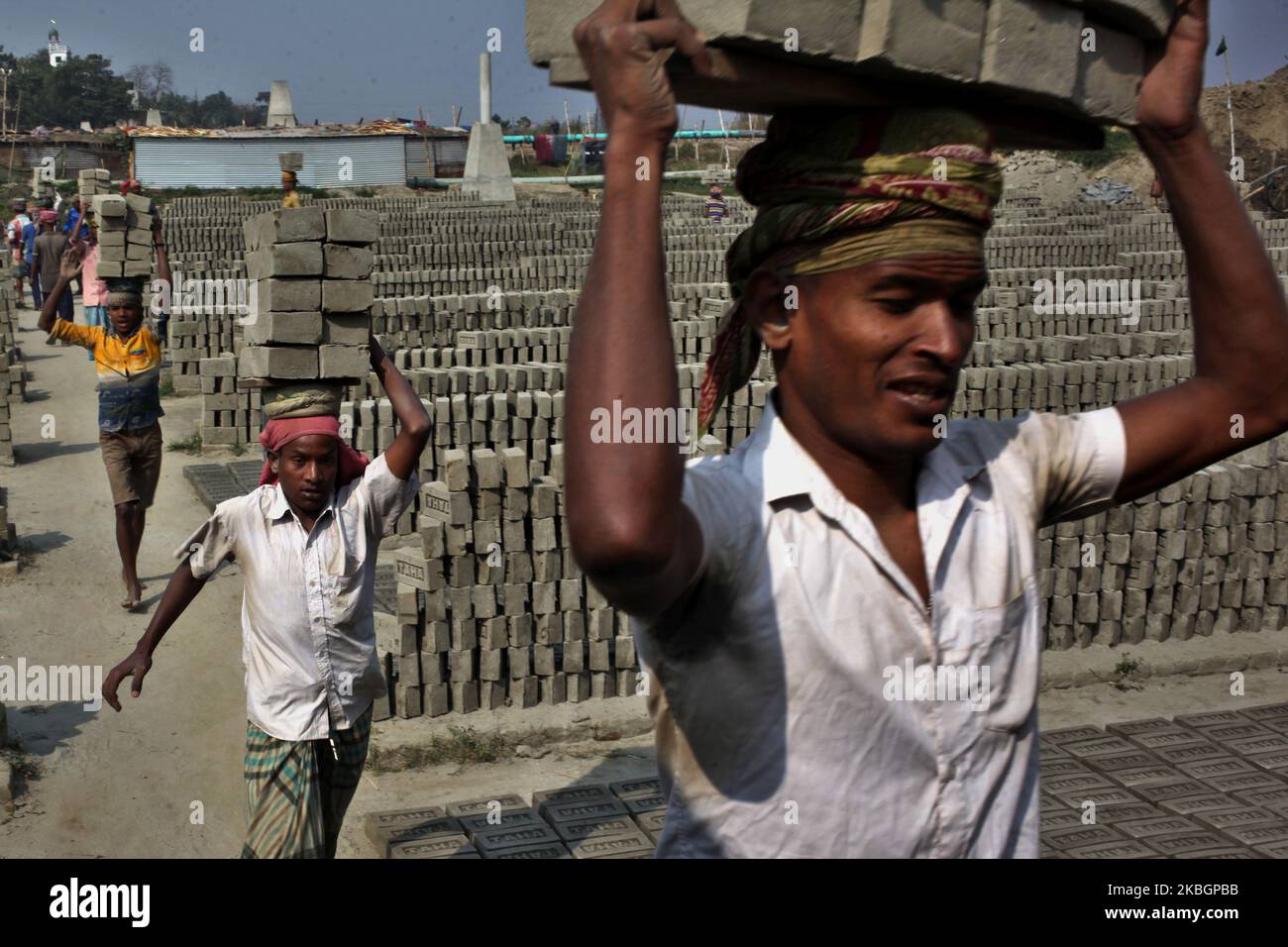 Workers carry raw bricks upon their head at a brick field near the ...