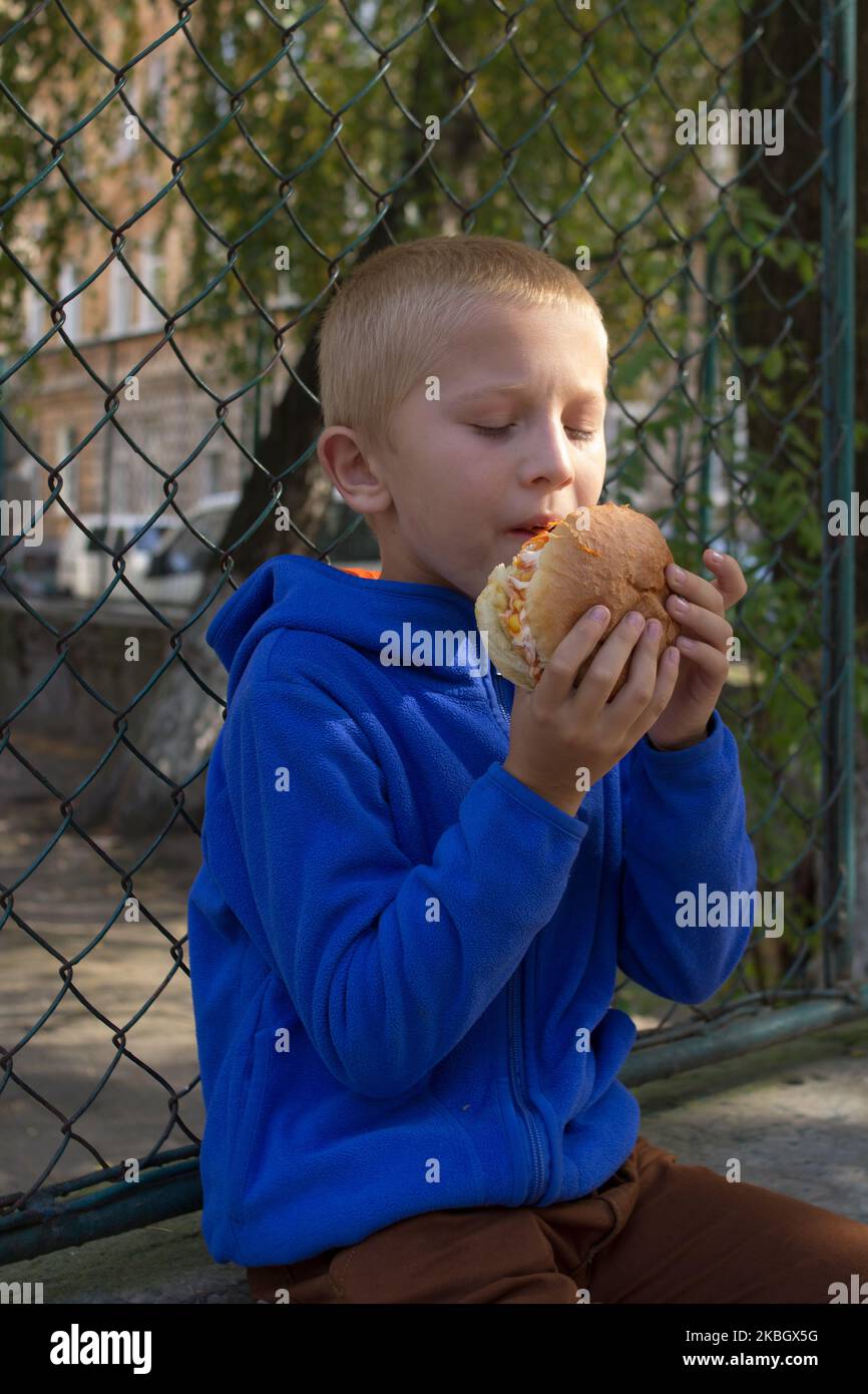 boy eats cheeseburger near fence grid near school Stock Photo - Alamy