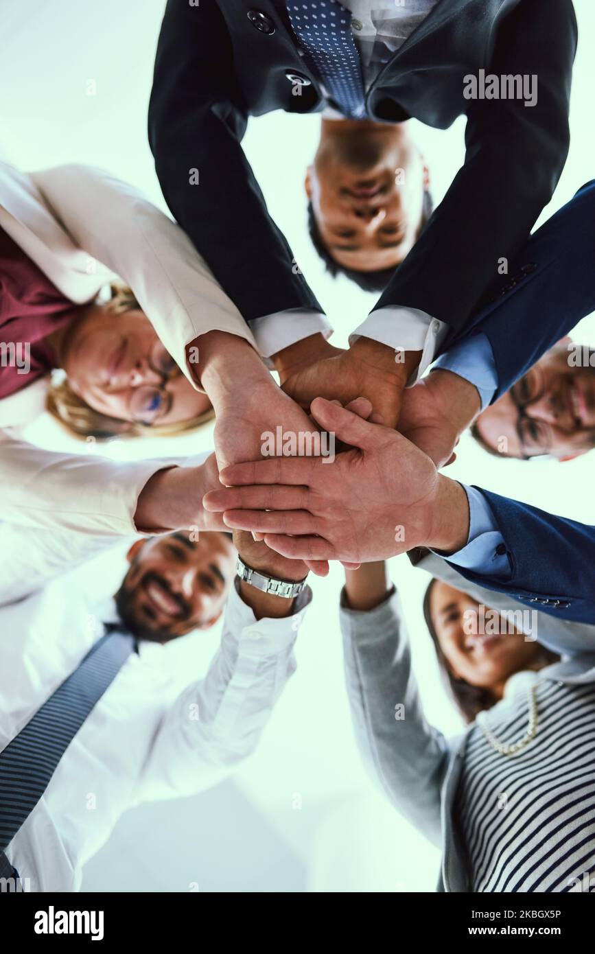 Going further together. Low angle shot of a diverse group of businesspeople joining their hands ...
