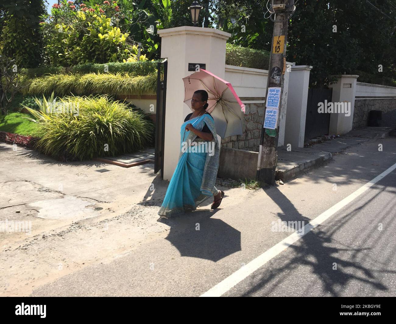 Woman walks along the roadside as she holds an umbrella to shade her ...