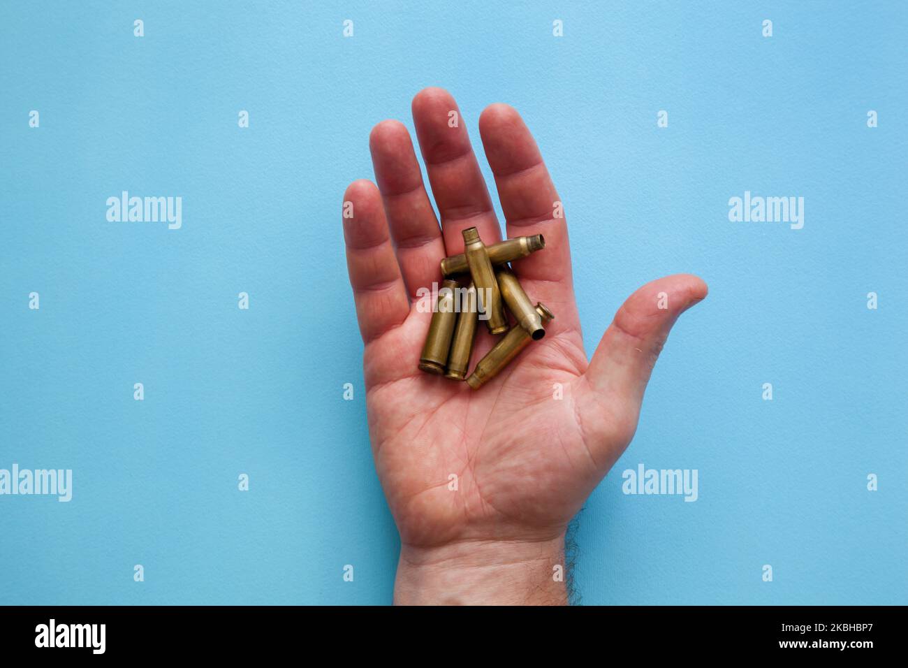 Empty cartridge cases in a male hand on a blue background. Army theme ...