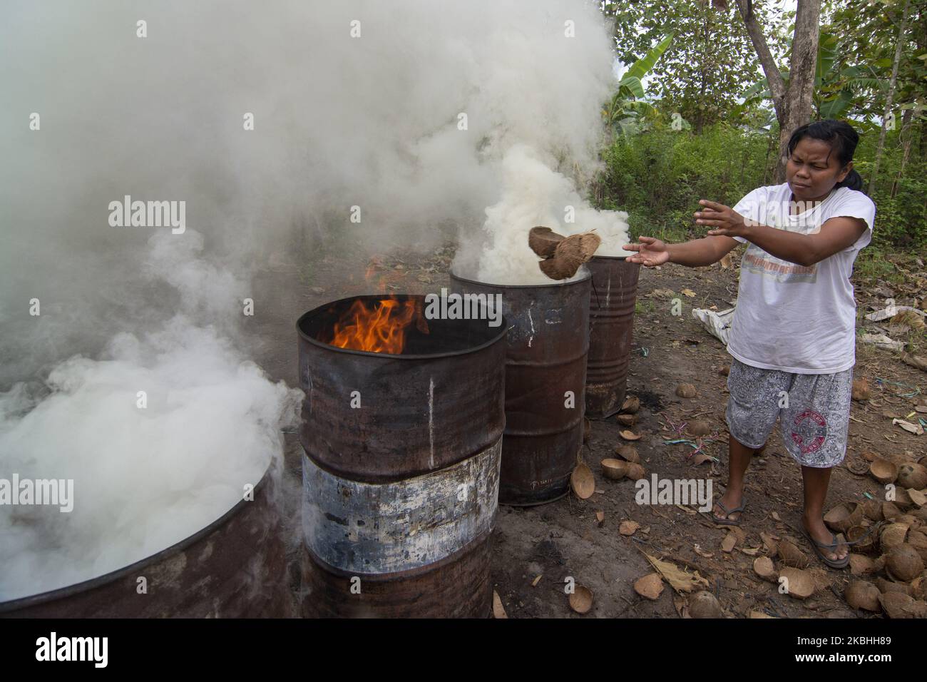 Worker put coconut shell into burning drums for charcoal making in the ...