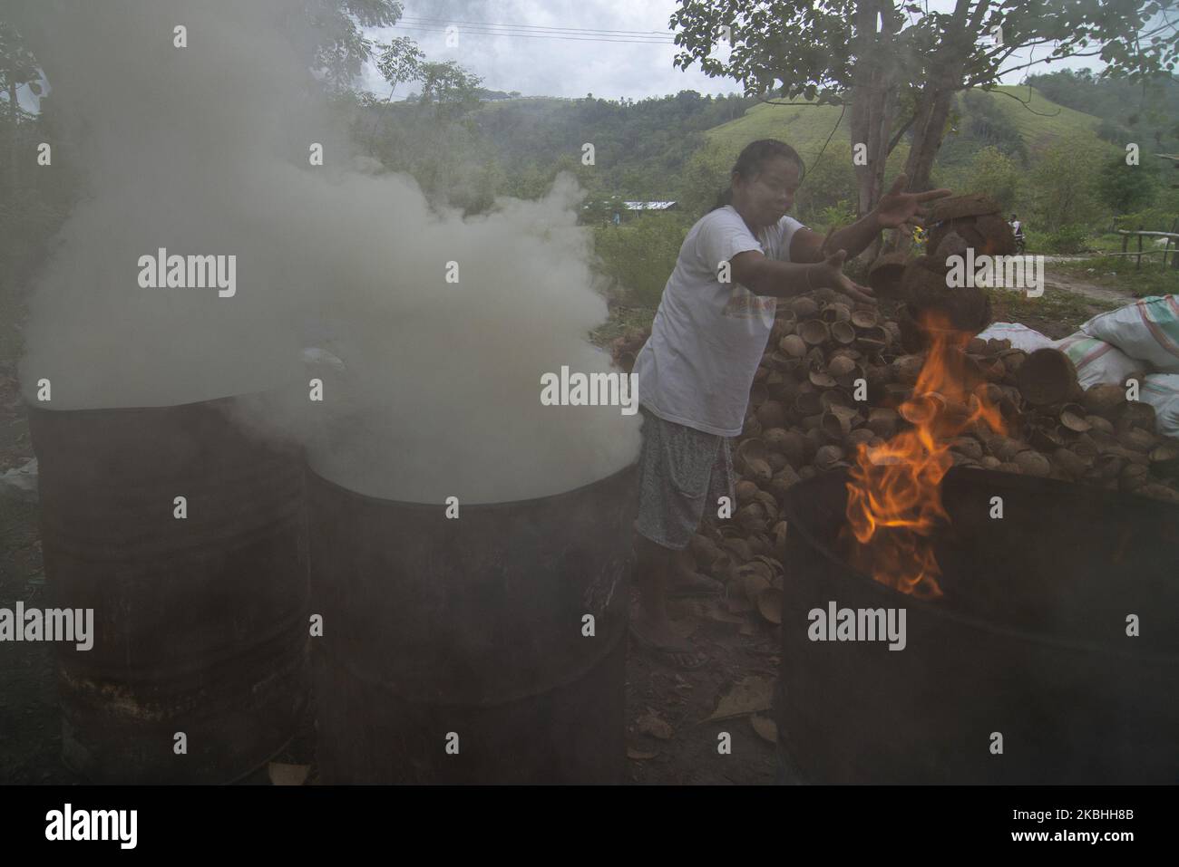 Worker put coconut shell into burning drums for charcoal making in the ...