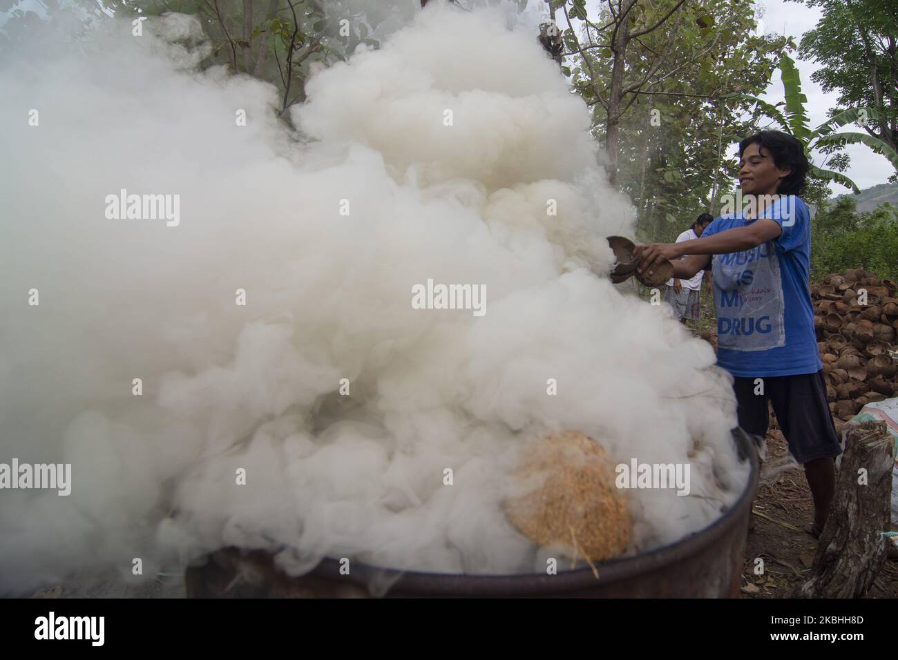 Worker put coconut shell into burning drums for charcoal making in the ...