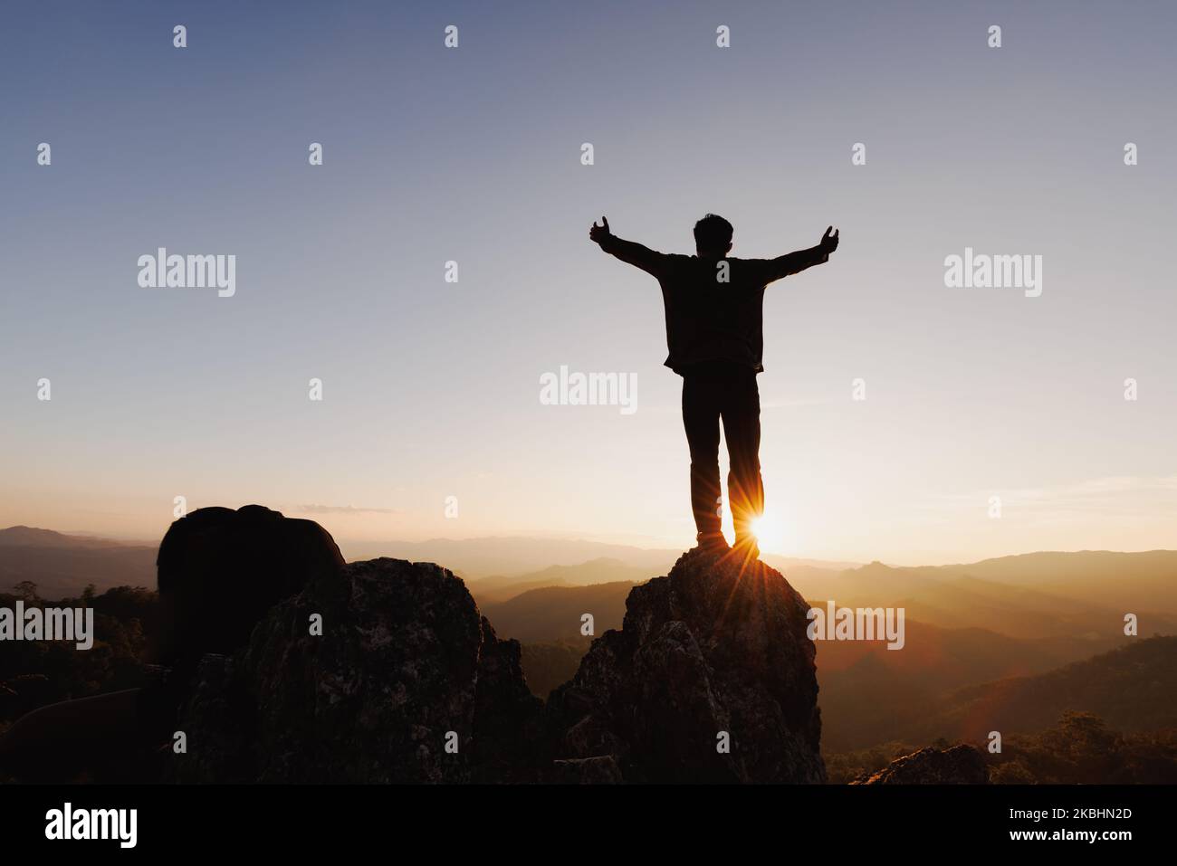 Silhouette of man rise hand up on top of mountain and sunset sky ...