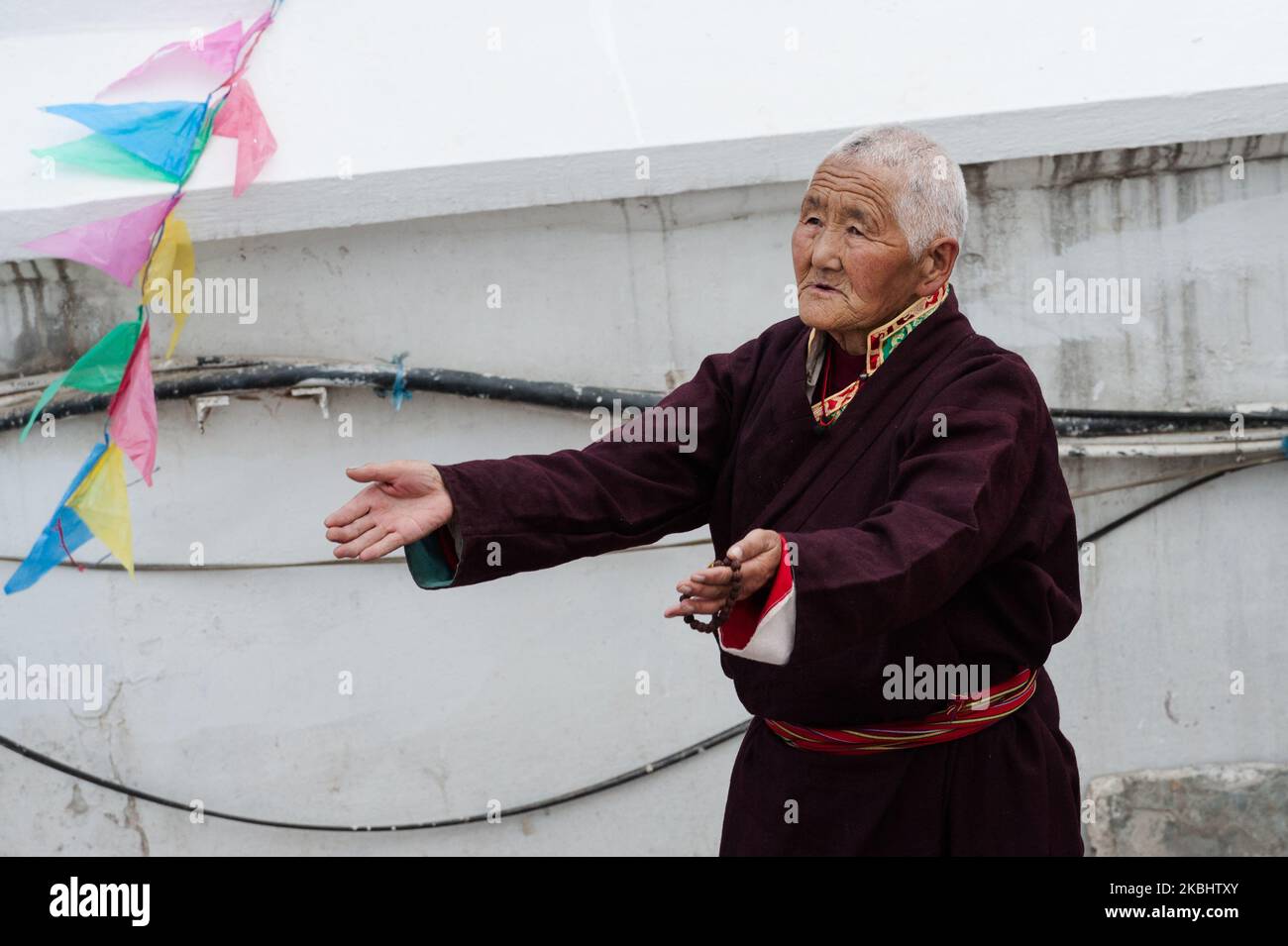 An old woman wearing Tibetan Buddhist maroon monk's robe prays at the ...