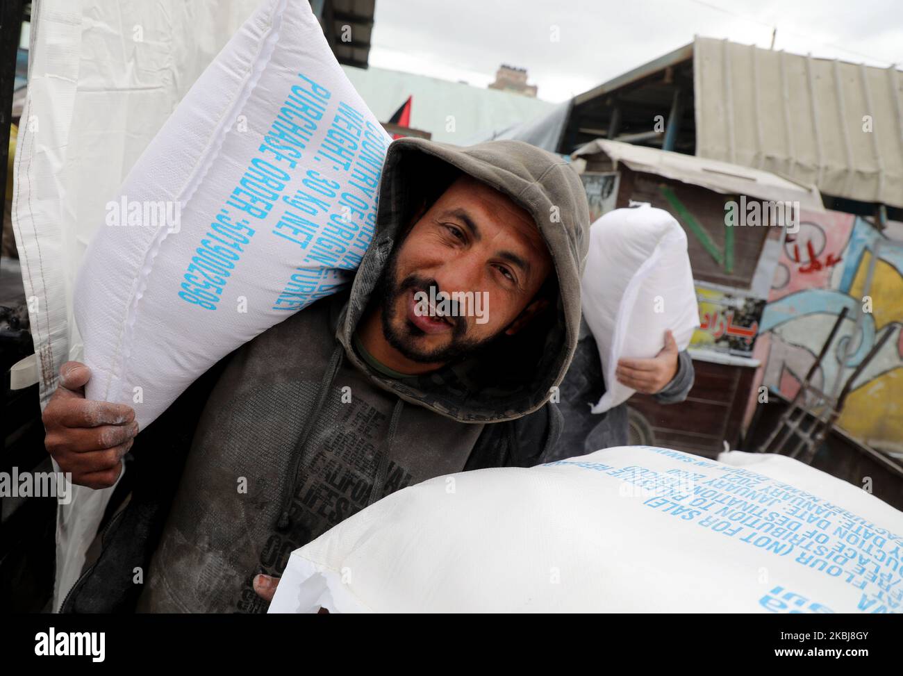 Palestinians carry sacks of flour as people receive food aid from a ...