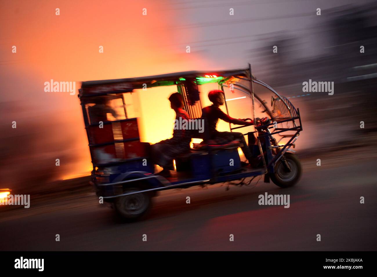An battery run auto rickshaw crosses a burning garbage beside a road at ...