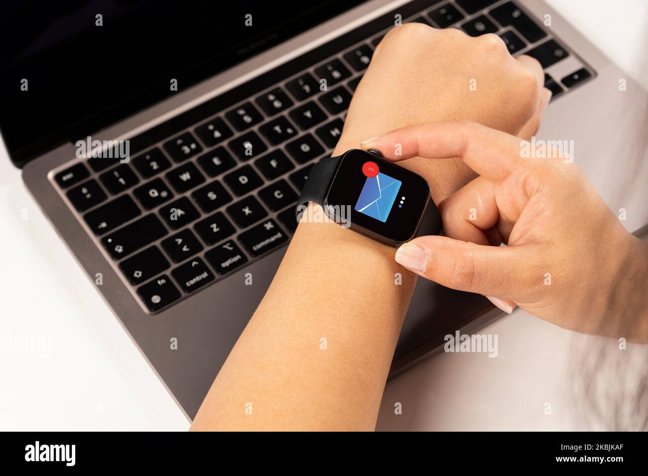 Email icon on smartwatch screen, woman hand over laptop touching email ...