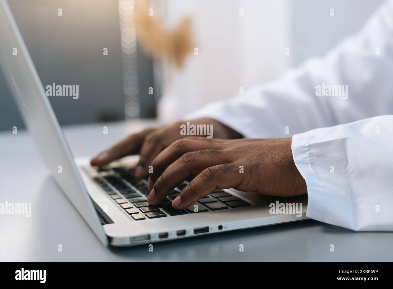 Close-up side view hands of unrecognizable African-American male doctor wearing white coat ...