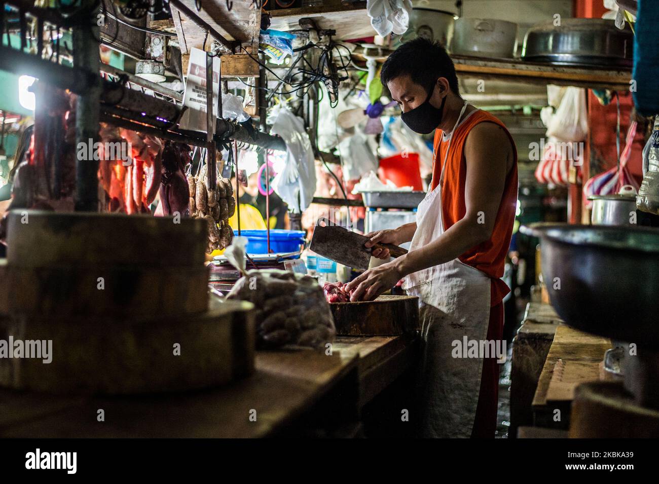 A meat vendor wearing a protective face mask chops pork in a market in ...