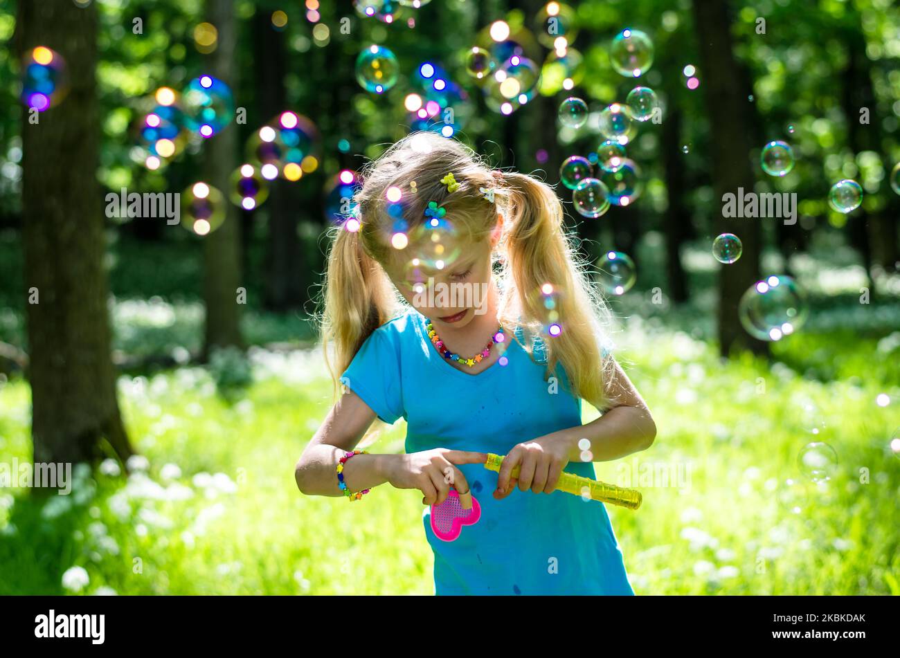 adorable blond girl having fun with soap bubbles outdoor in green ...