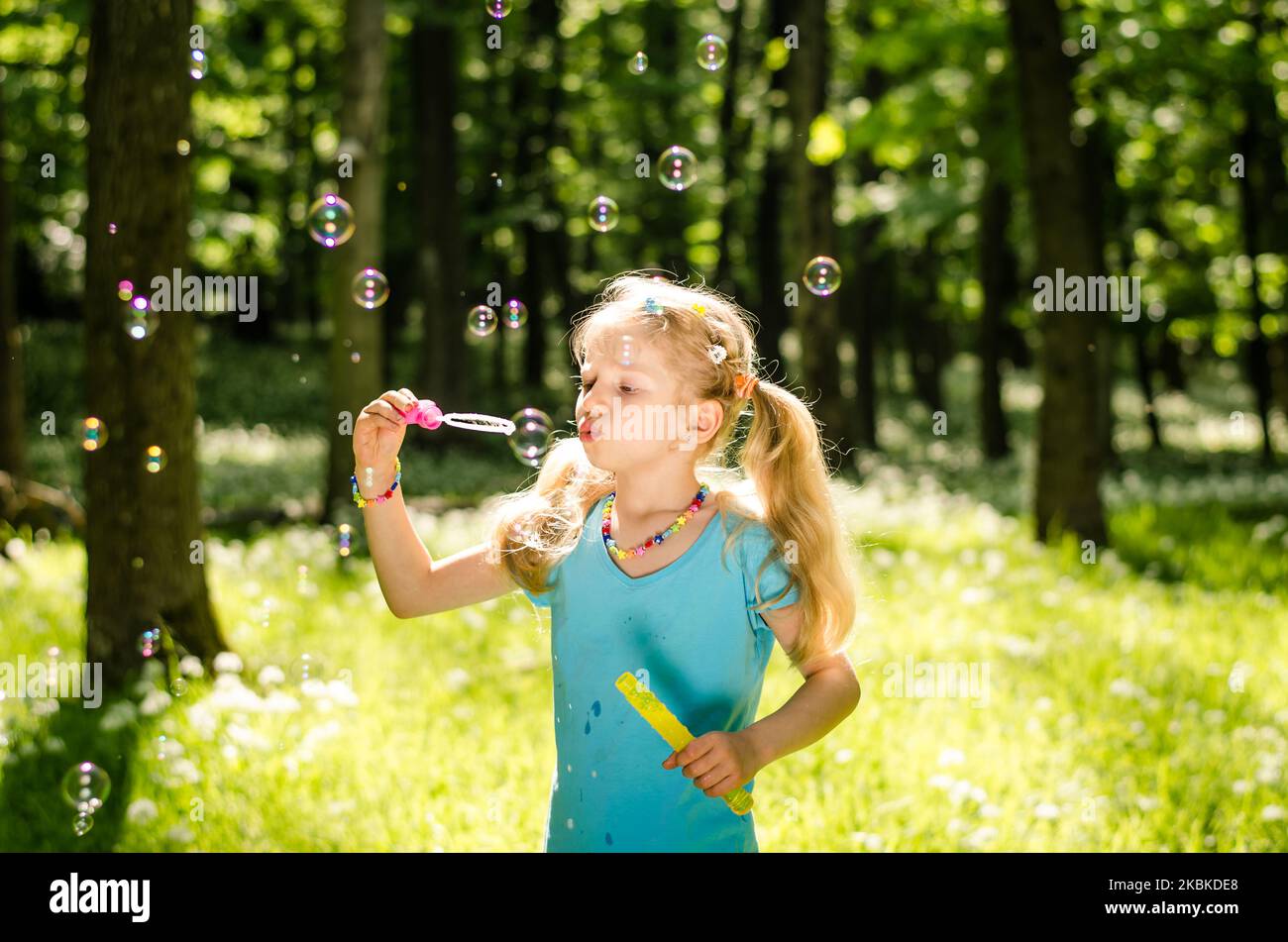 adorable blond girl having fun with soap bubbles outdoor in green ...