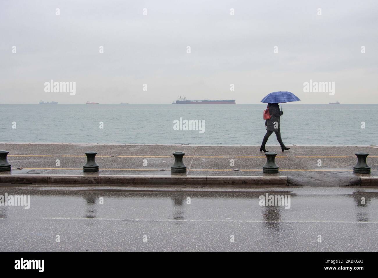 A woman walking alone holding an umbrella, as seen in the waterfront ...