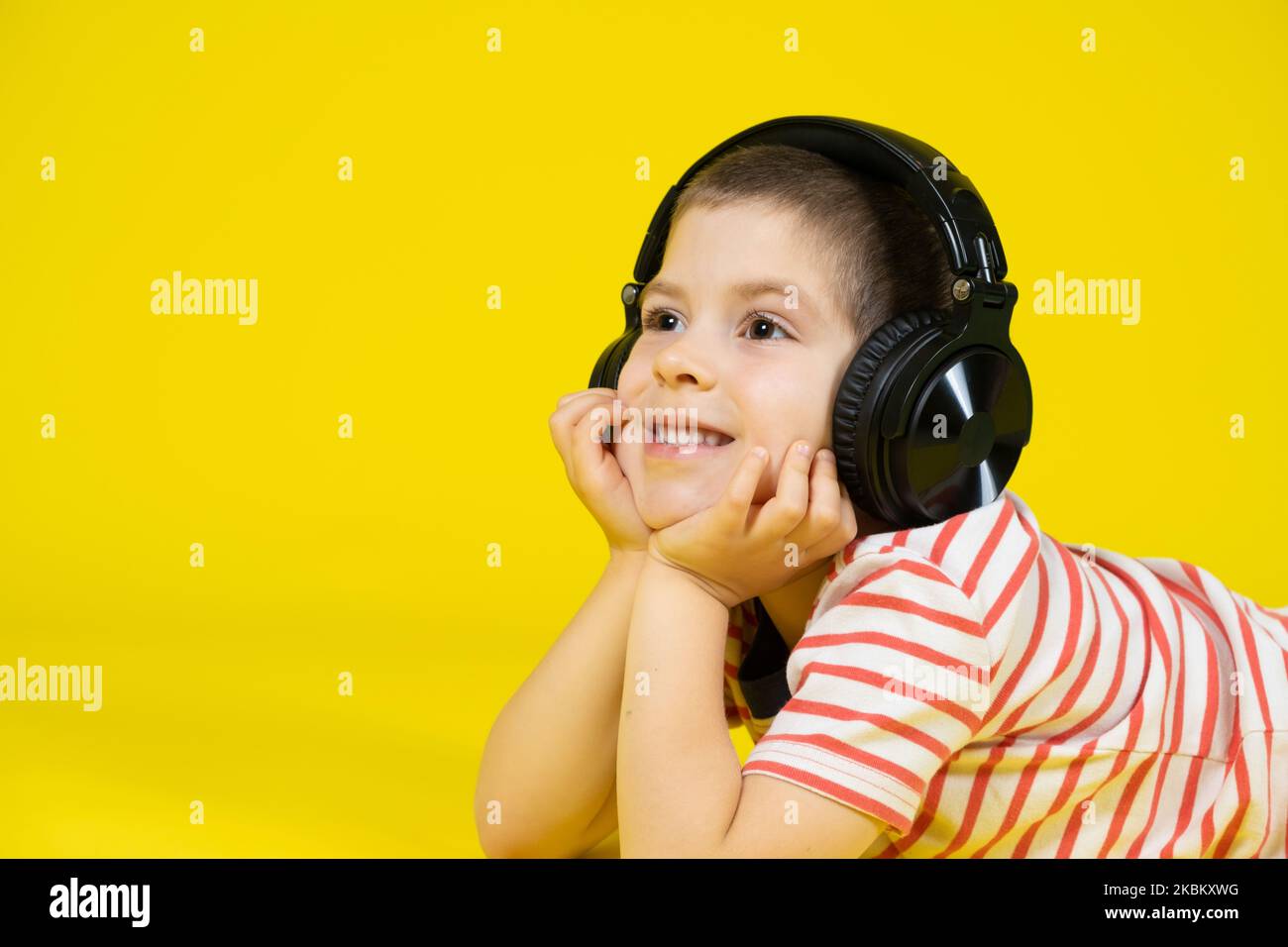 Cute 5 year old boy in wireless large headphones lies on a yellow ...