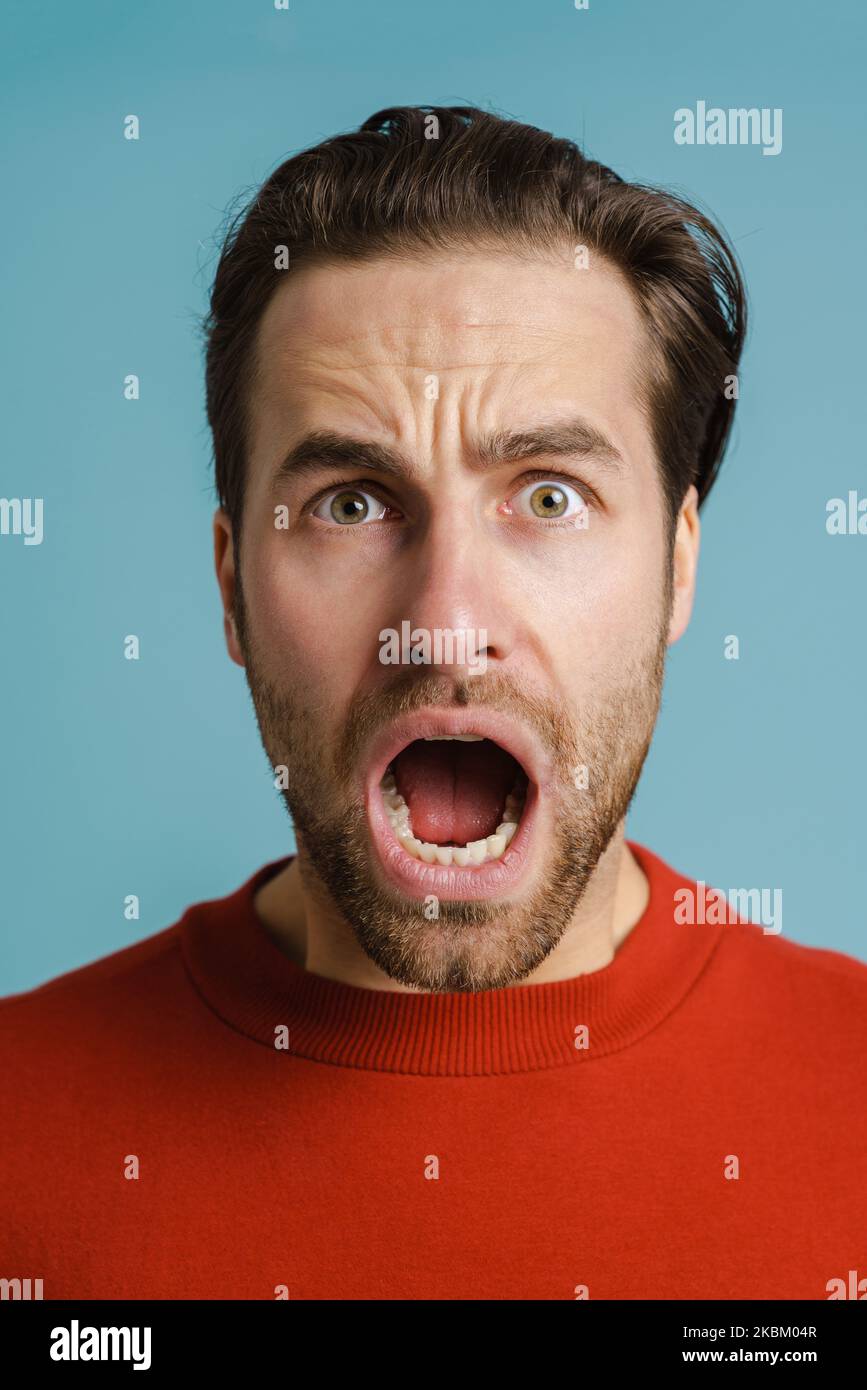 Young shocked man wearing red sweater screaming at camera isolated over ...