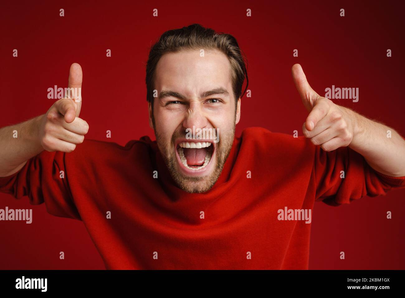 Young bristle man screaming and pointing fingers at camera isolated ...