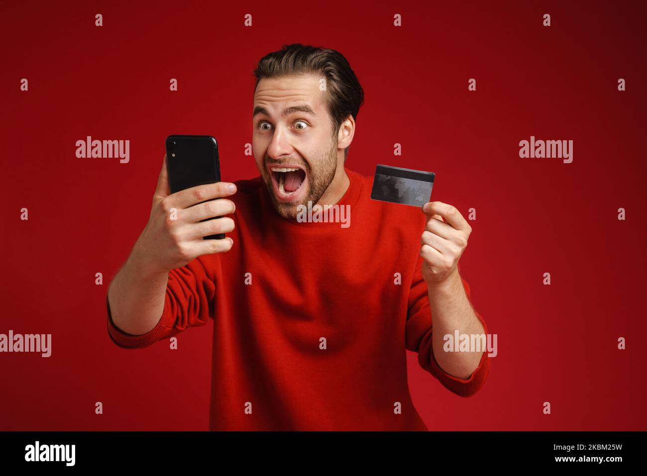 Young shocked man screaming while using cellphone and credit card ...