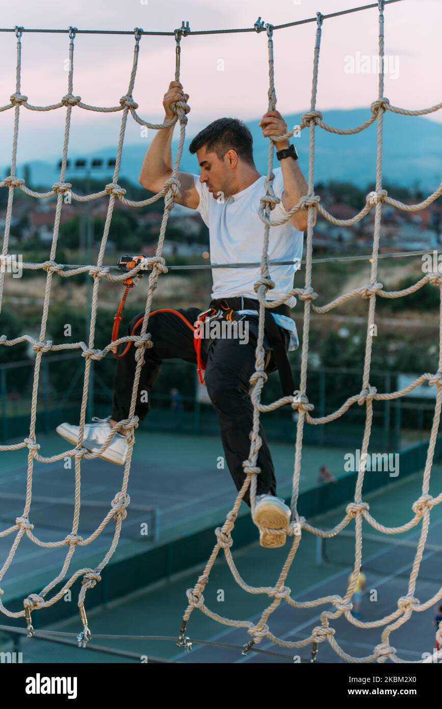 Adventure man climbing the rope at the adventure park Stock Photo - Alamy