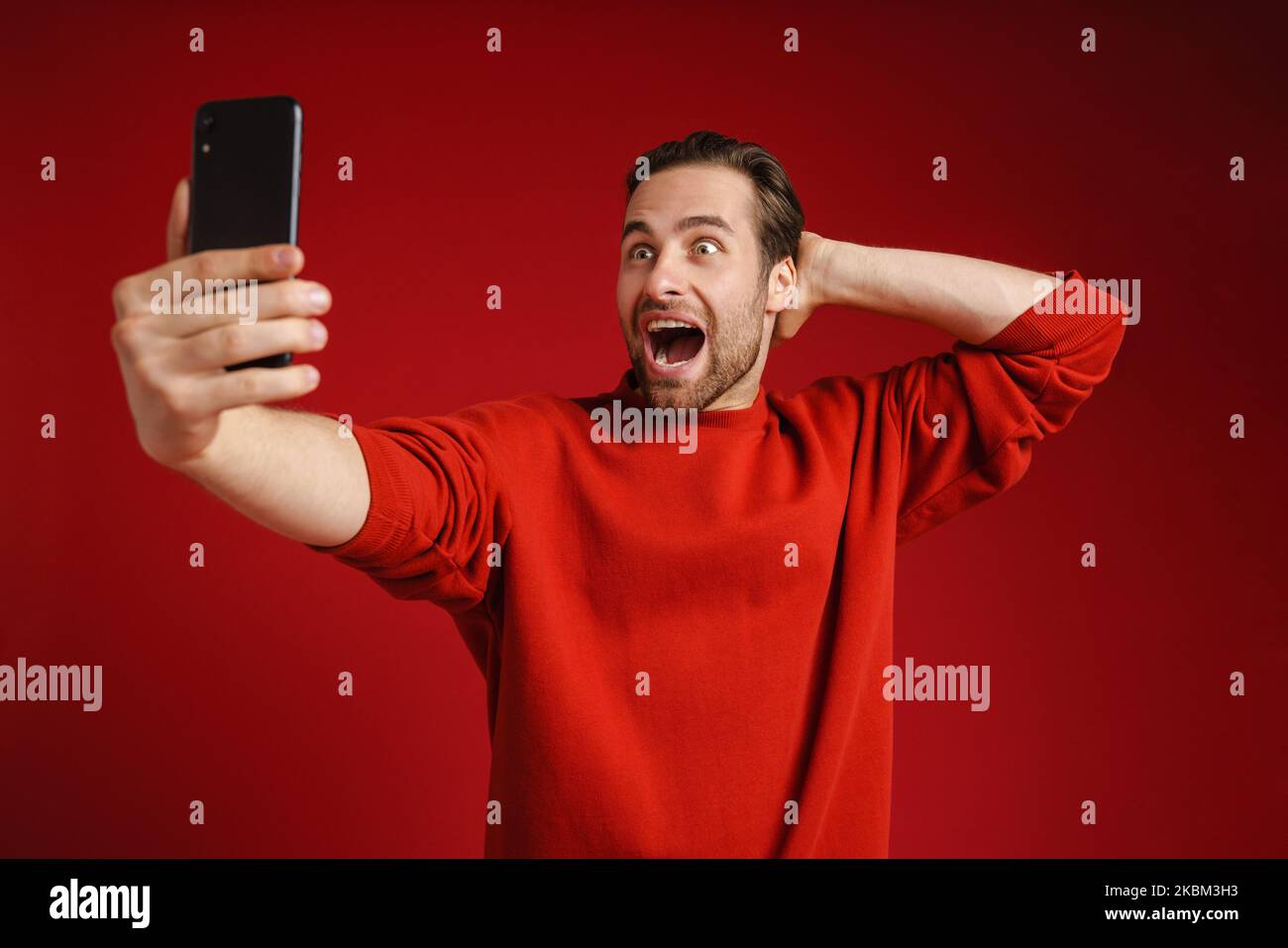 Young man expressing surprise while taking selfie on cellphone isolated ...