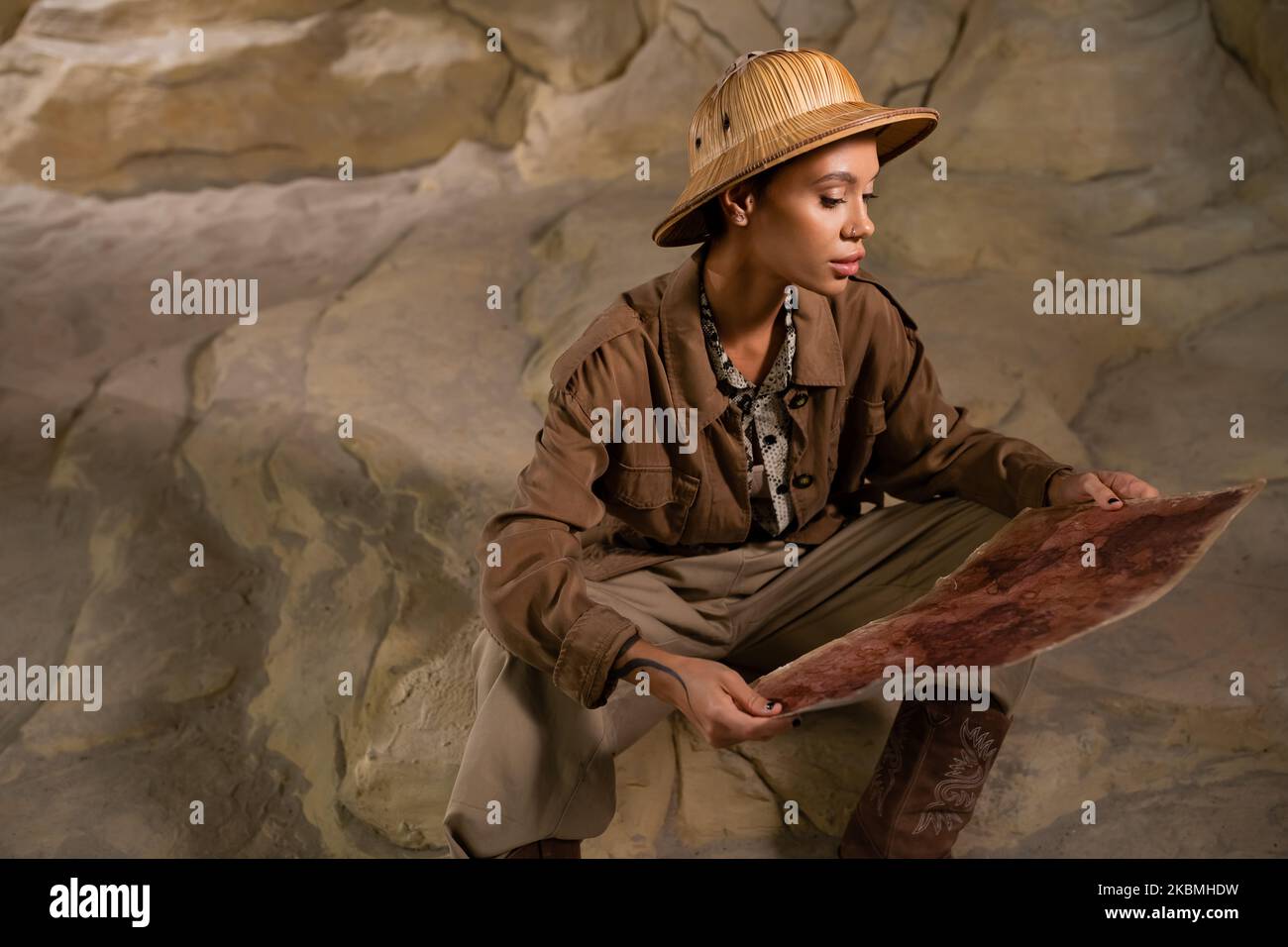 young archaeologist in safari style outfit sitting on rock and looking ...