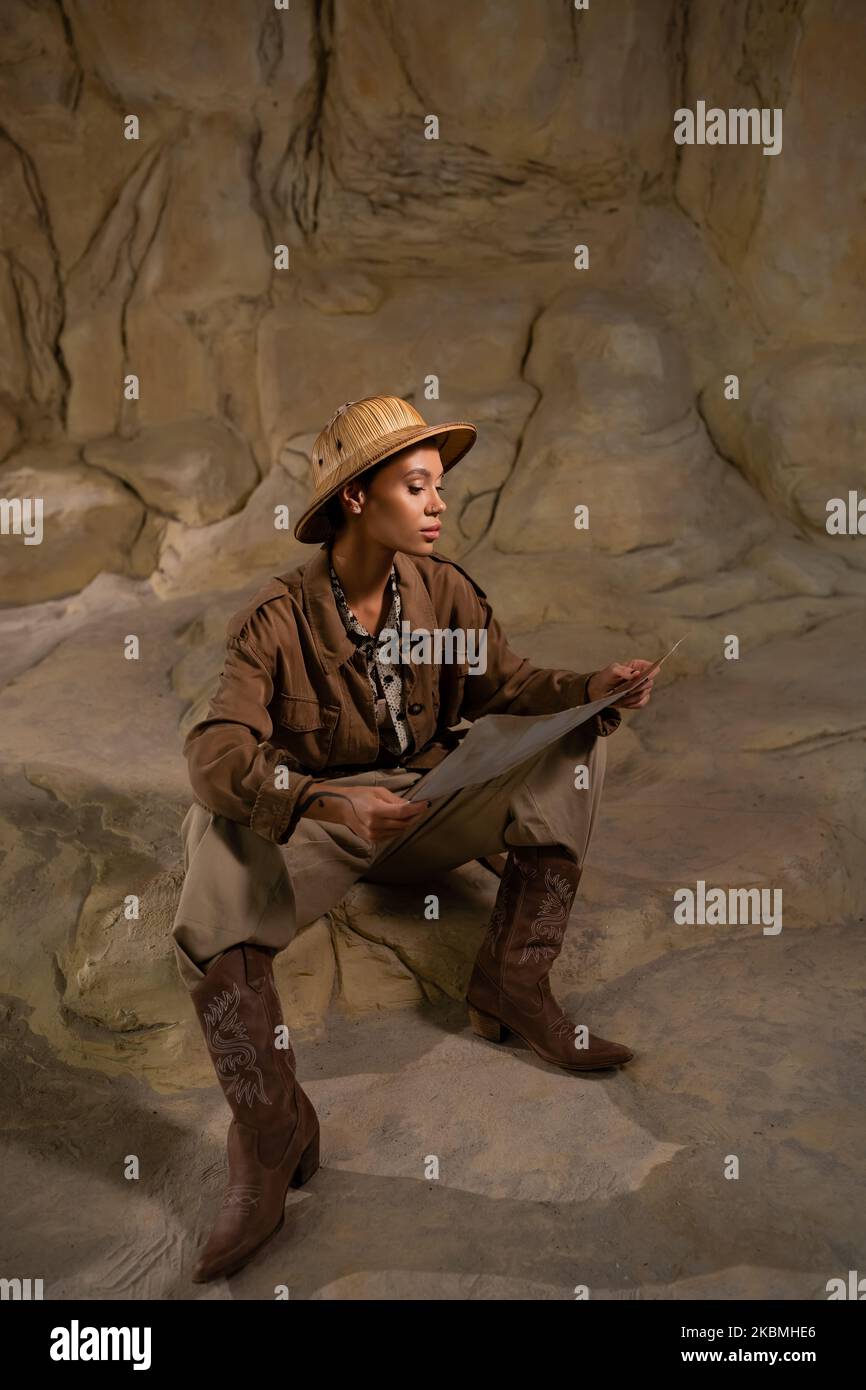 archaeologist in safari hat and cowboy boots looking at ancient map in ...