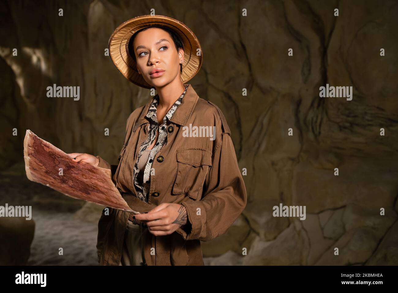 young archaeologist in safari hat holding ancient map and looking away ...