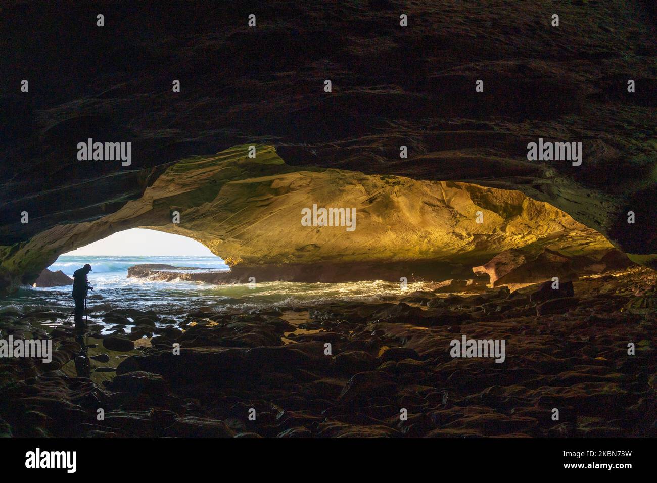 Tourist exploring Waenhuiskrans sea-cave, gazing towards the cave mouth ...