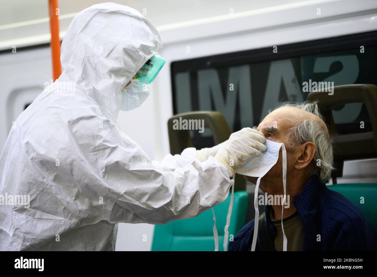 A health worker adjusts a face mask to an elderly man as being ...