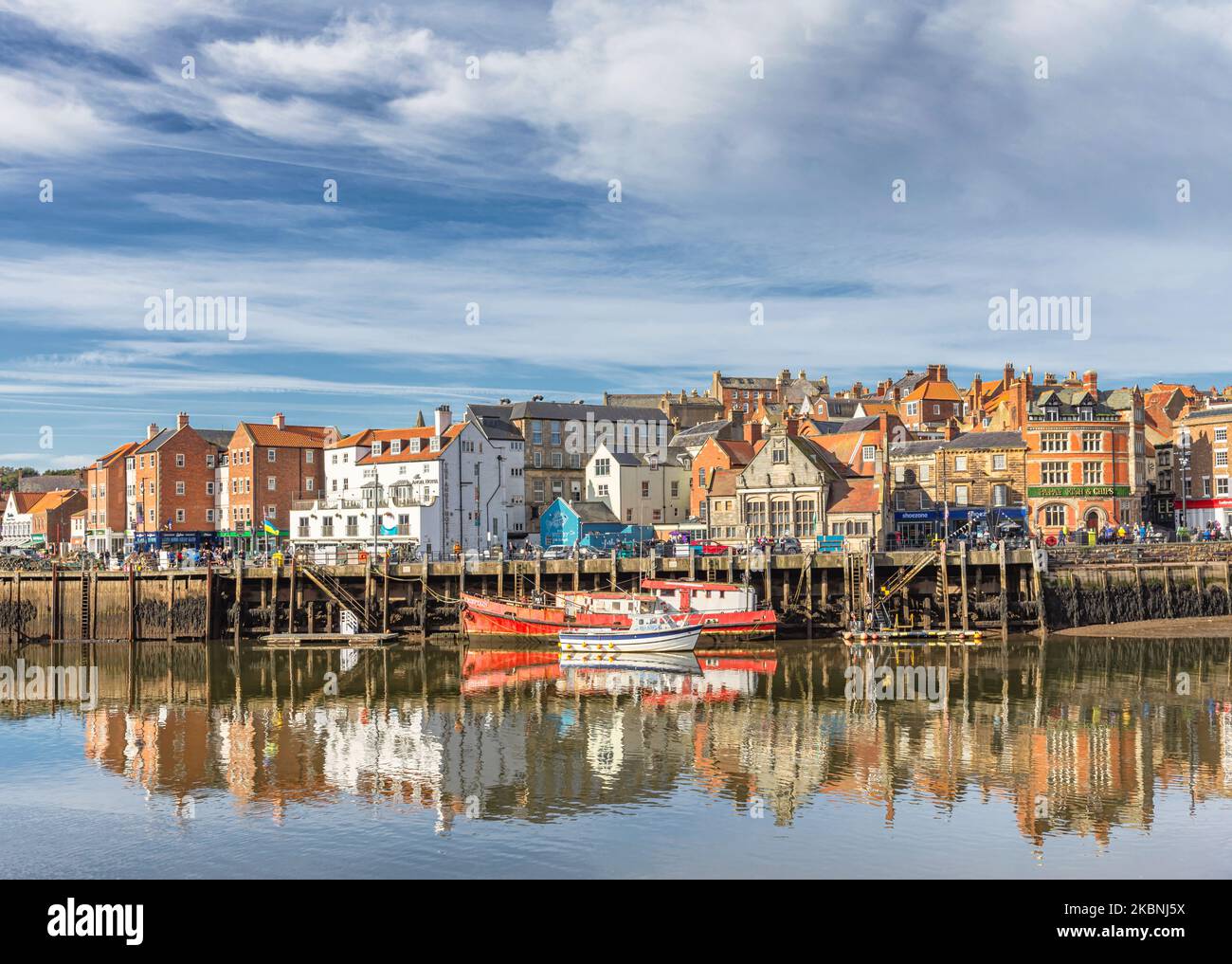 Whitby harbour with town buildings lining the waterfront. Boats are ...