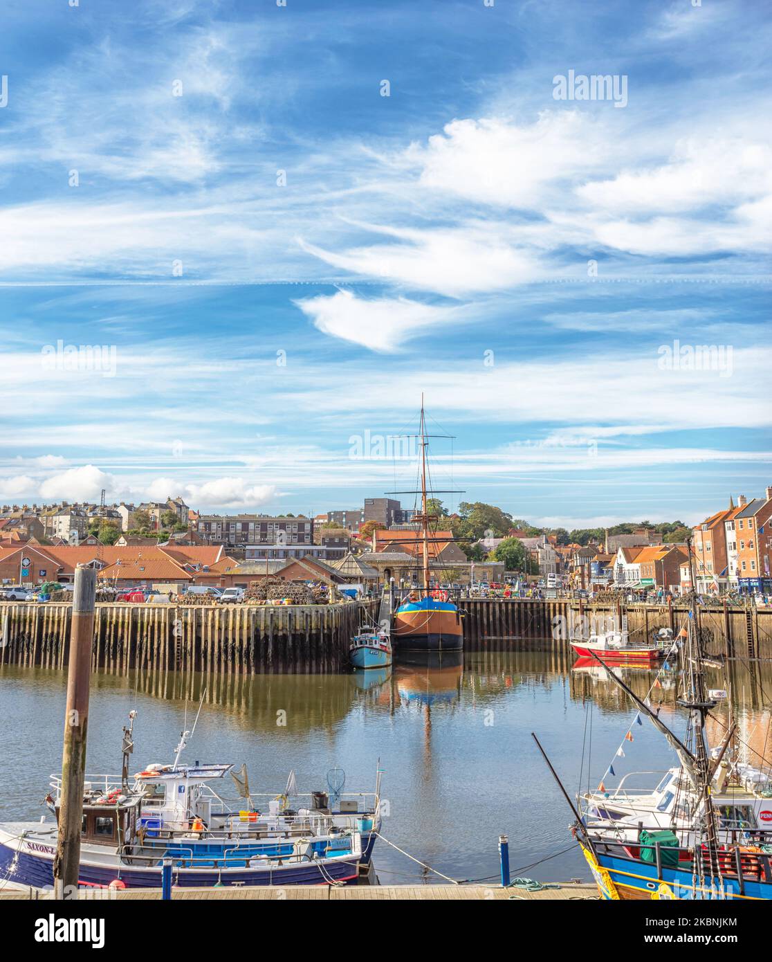 Whitby harbour with a tall ship moored at a quay. Buildings line the ...