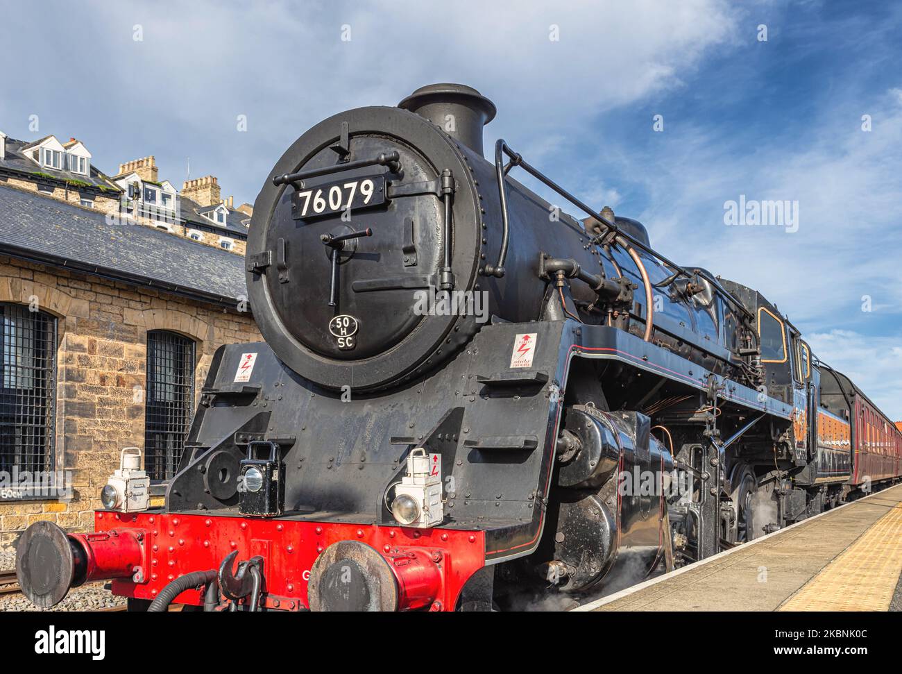 A polished black steam locomotive stands at a platform. Steam emits ...