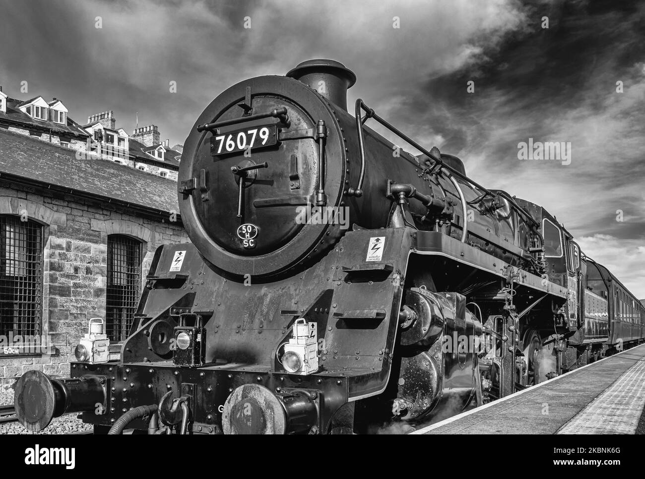 A polished black steam locomotive stands at a platform. Steam emits ...