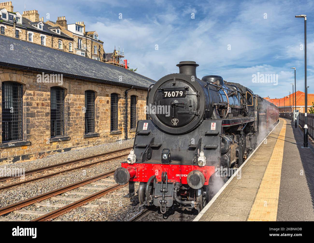 A polished black steam locomotive stands at a platform. Steam emits ...