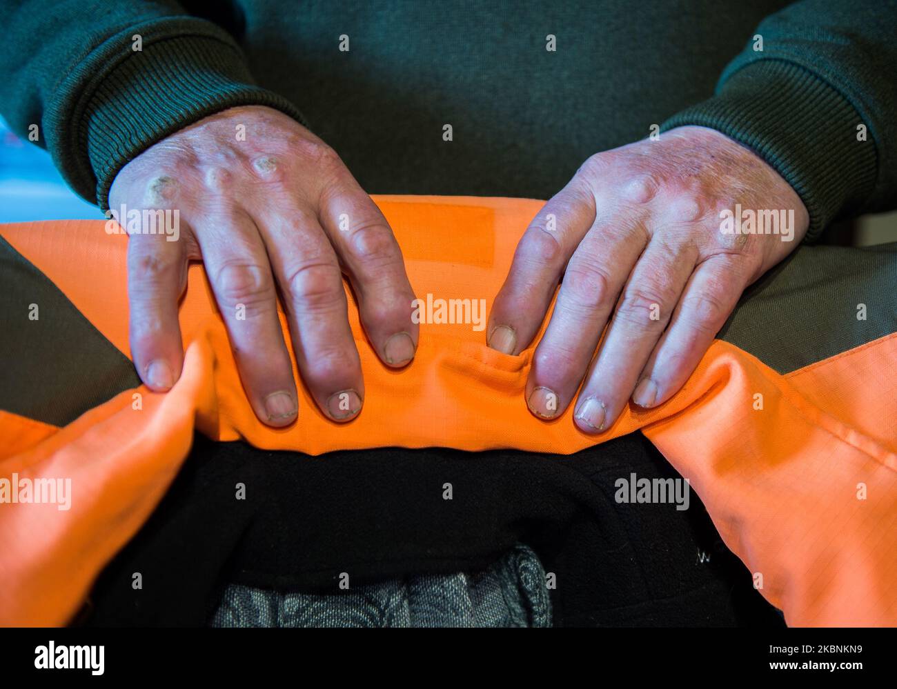 Hands of an old man, hunter’s hands in front of his orange hunting vest ...